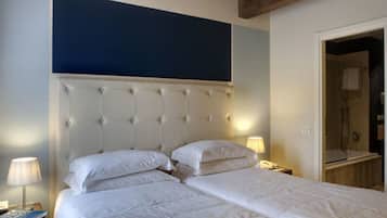 Uma cama de casal com cabeceira estofada, duas luminárias de cabeceira e uma mesinha de noite com um livro e um abajur.