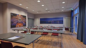 Sala de conferências com mesas, cadeiras e obras de arte nas paredes.