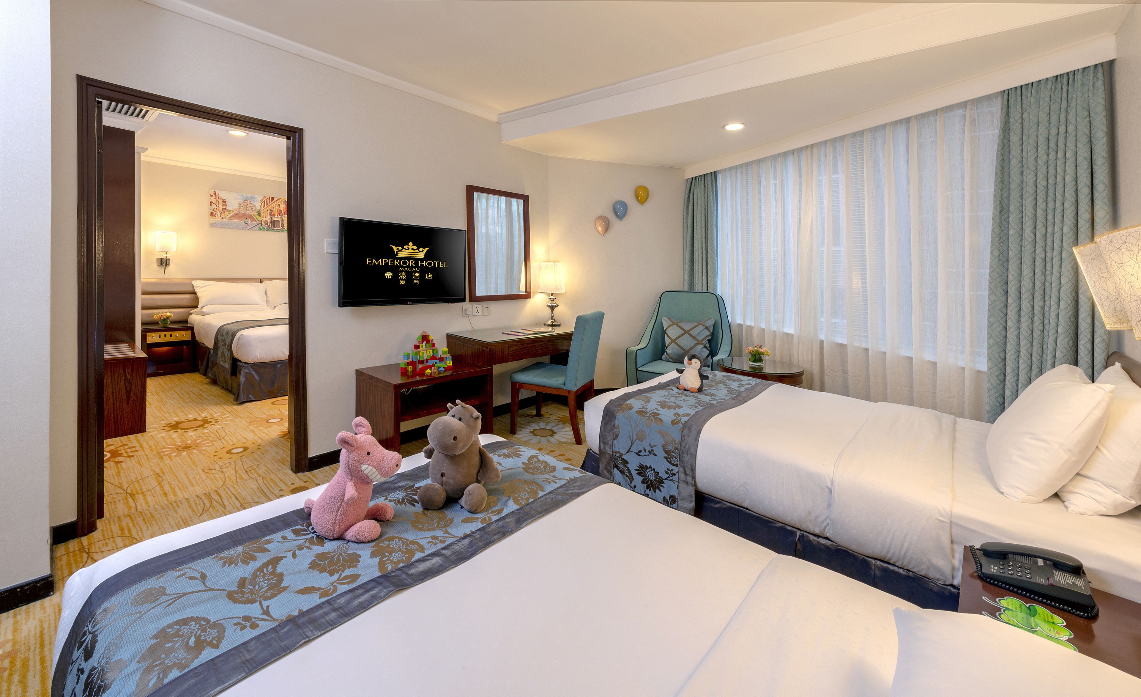 Quarto de hotel com duas camas, uma escrivaninha, uma cadeira, uma televisão e um espelho.