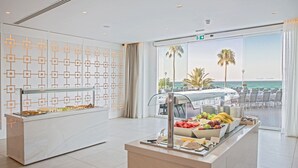Uma área de buffet com balcão de mármore, vitrine de vidro e vista para o oceano através de grandes janelas.