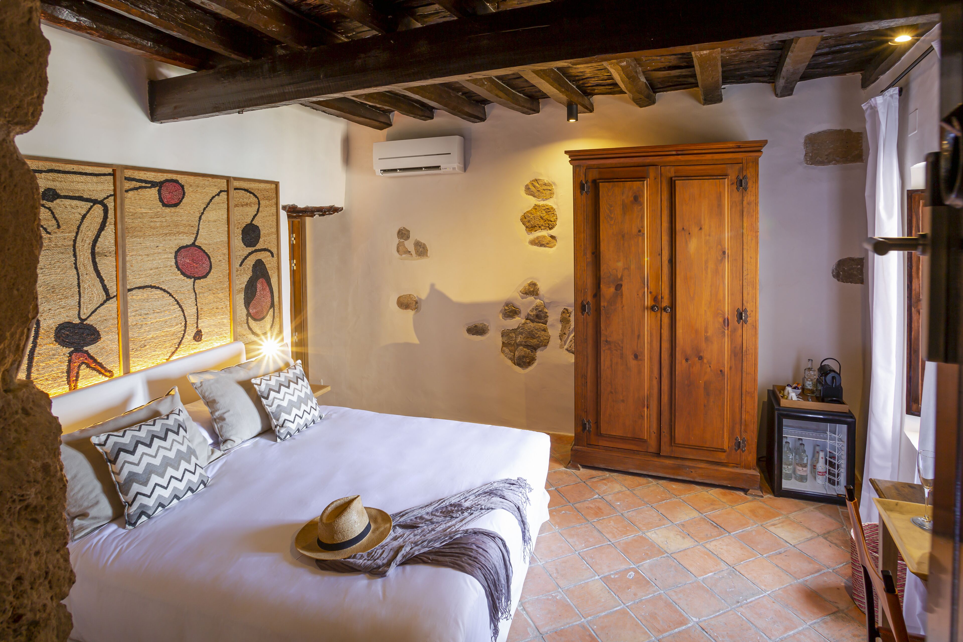 Quarto com cama, guarda-roupa de madeira, parede decorada com pedras e ar condicionado.