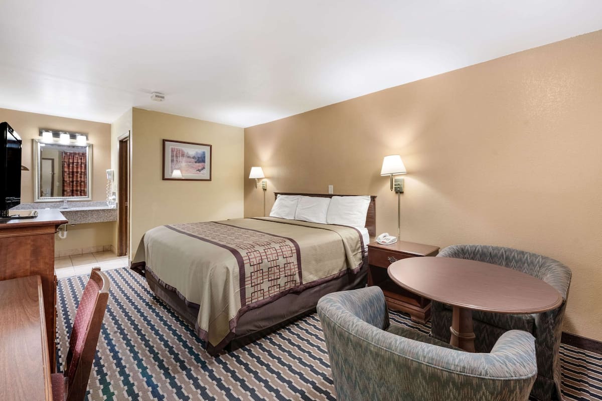 Quarto de hotel com cama, mesa de cabeceira, cadeira e uma pequena mesa redonda.