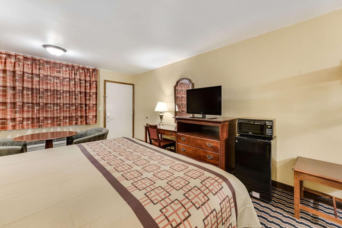 Quarto de hotel com uma cama grande, uma escrivaninha, uma televisão, um micro-ondas e uma pequena mesa.