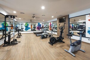 Academia com equipamentos de cardio, aparelhos de musculação e espelhos nas paredes.