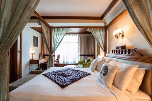 Uma cama bem arrumada com um cobertor estampado, uma mesa de cabeceira com abajur e vista para uma varanda com cortinas.