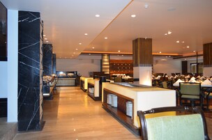 Um hall de hotel moderno com colunas de mármore, um balcão de recepção e uma área de jantar com mesas e cadeiras.