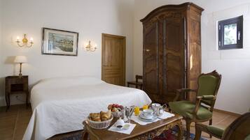 Quarto bem arrumado com cama, bandeja de café da manhã, guarda-roupa de madeira e uma poltrona verde.