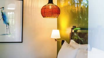 Quarto de hotel com cama, obra de arte emoldurada de um pássaro, luminária pendente vermelha e preta, e luminária fixada na parede.