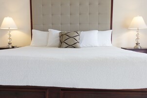 Uma cama grande com cabeceira estofada, duas luminárias de apoio e um travesseiro decorativo.
