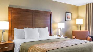 Quarto de hotel com uma cama grande, duas mesas de cabeceira com abajures, uma cadeira e um quadro na parede.