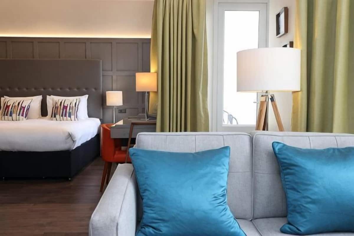 Quarto de hotel com cama, sofá, escrivaninha e luminária.