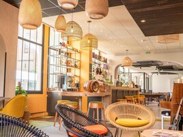Uma área de bar com móveis de vime, prateleiras com garrafas e uma janela grande.