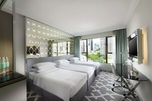 Quarto de hotel com duas camas, uma escrivaninha, uma TV e uma janela grande com vista para a cidade.