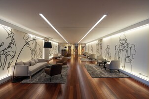 Um hall de hotel moderno com área de estar central, piso de madeira e grandes obras de arte nas paredes.