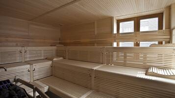 Uma sala de sauna com bancos e bancos de madeira, uma mesa de sauna e uma janela com persianas.