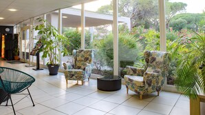 Um espaço amplo e interno, com grandes janelas, cadeiras modernas e plantas em vasos.
