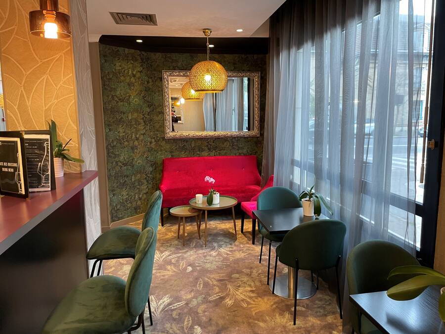 Um interior acolhedor com um sofá vermelho, cadeiras verdes, uma mesinha redonda e um espelho na parede.