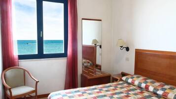 Quarto de hotel com uma cama, uma cadeira, uma mesa de cabeceira, um espelho e uma janela com vista para o mar.