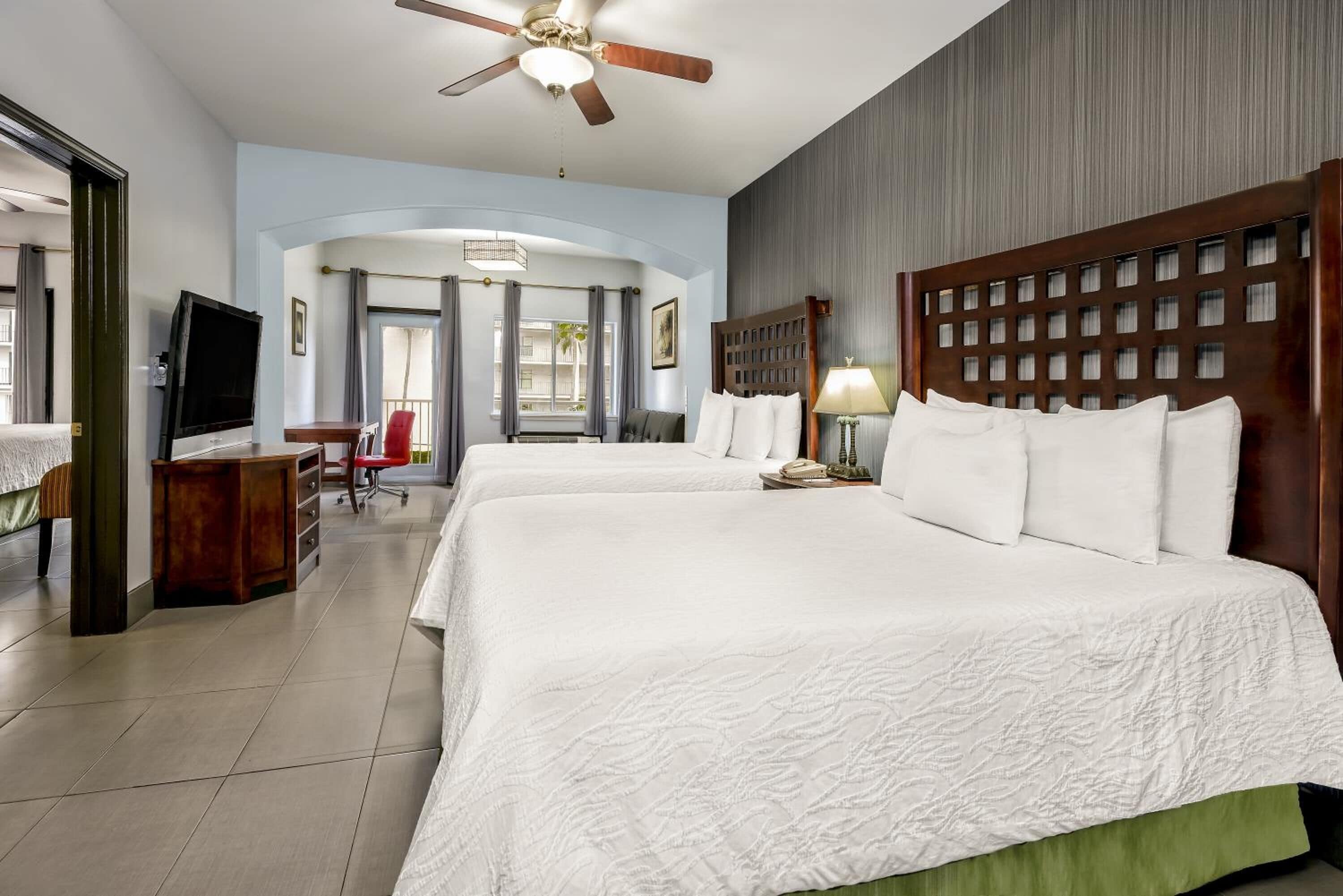 Quarto de hotel com duas camas, televisão, escrivaninha e ventoinha no teto.