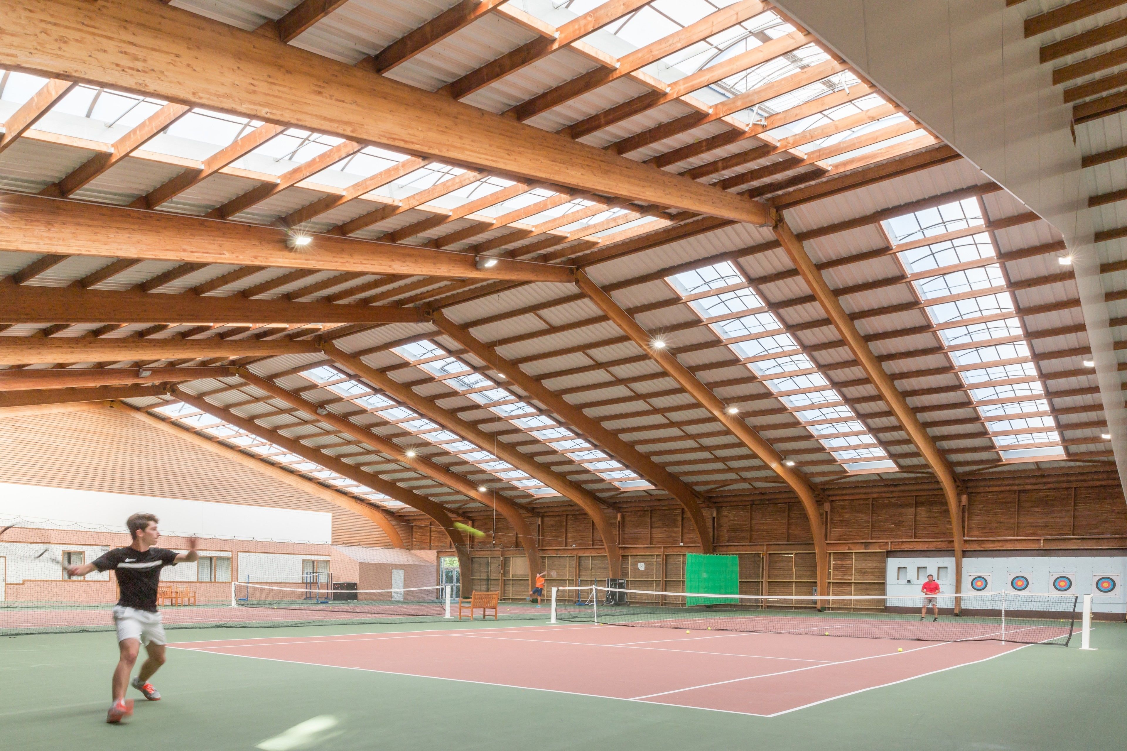 Uma quadra de tênis interna com teto de madeira alto e uma rede no centro.