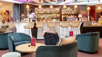 Uma área de bar com balcão, banquetas e um espaço de estar com sofás e uma mesa redonda.