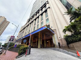Um edifício moderno com entrada destacada, toldo azul e placa indicando uma saída.