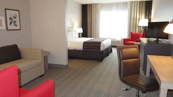 Quarto de hotel com uma cama, escrivaninha, poltrona, sofá e televisão.
