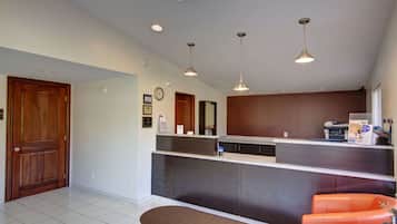 Uma área de recepção com porta de madeira, balcão de atendimento, cadeira acolchoada marrom e luminárias pendentes.