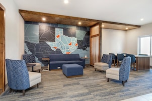 Um hall de entrada com um sofá azul, poltronas combinando, uma mesa pequena e um mural com um mapa na parede.