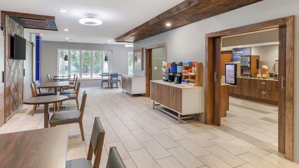 Um lobby de hotel moderno com piso de madeira, área de recepção e espaço de refeições com mesas e cadeiras.