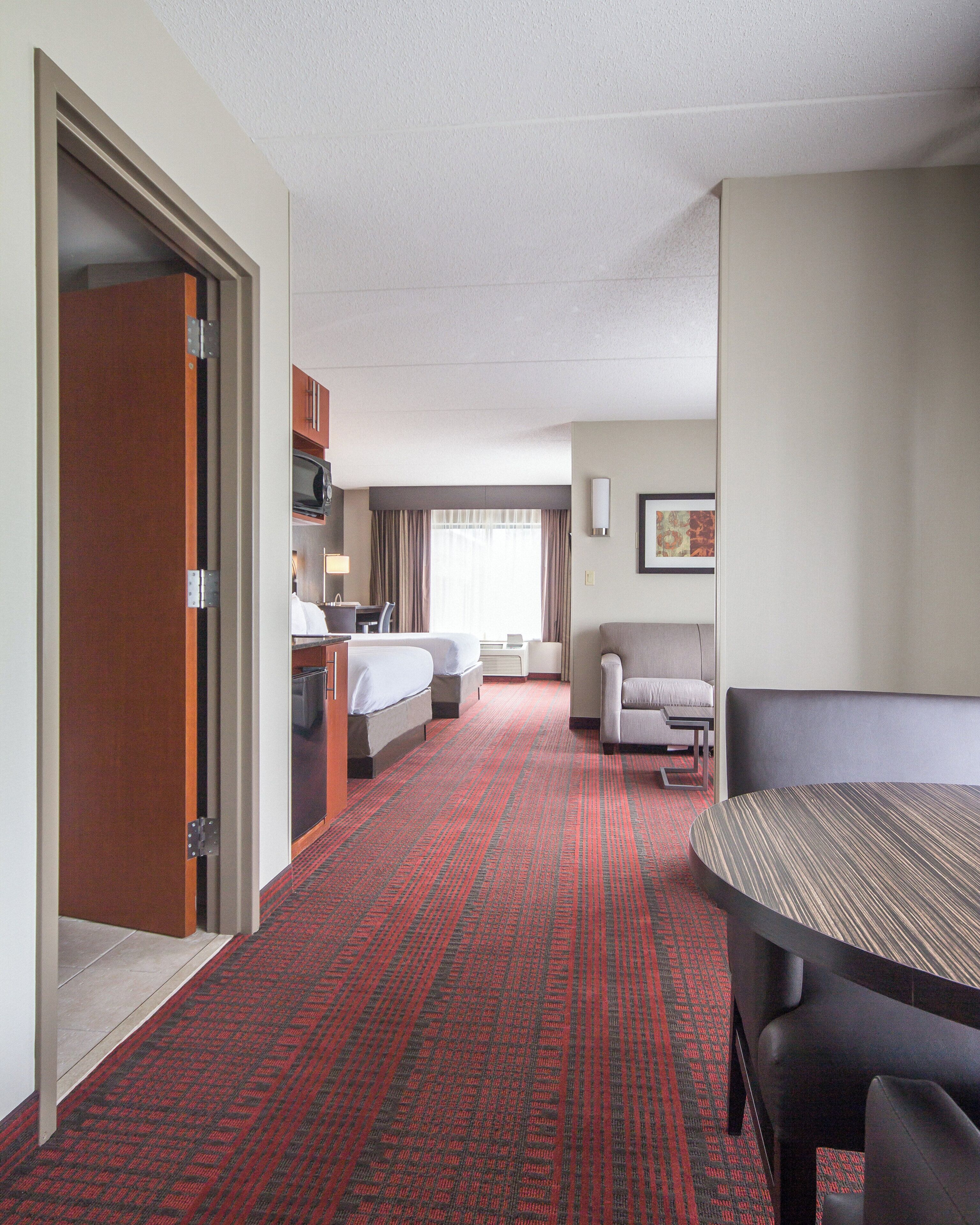 Quarto de hotel com cama, escrivaninha, cadeira, mesa e piso coberto por carpete.