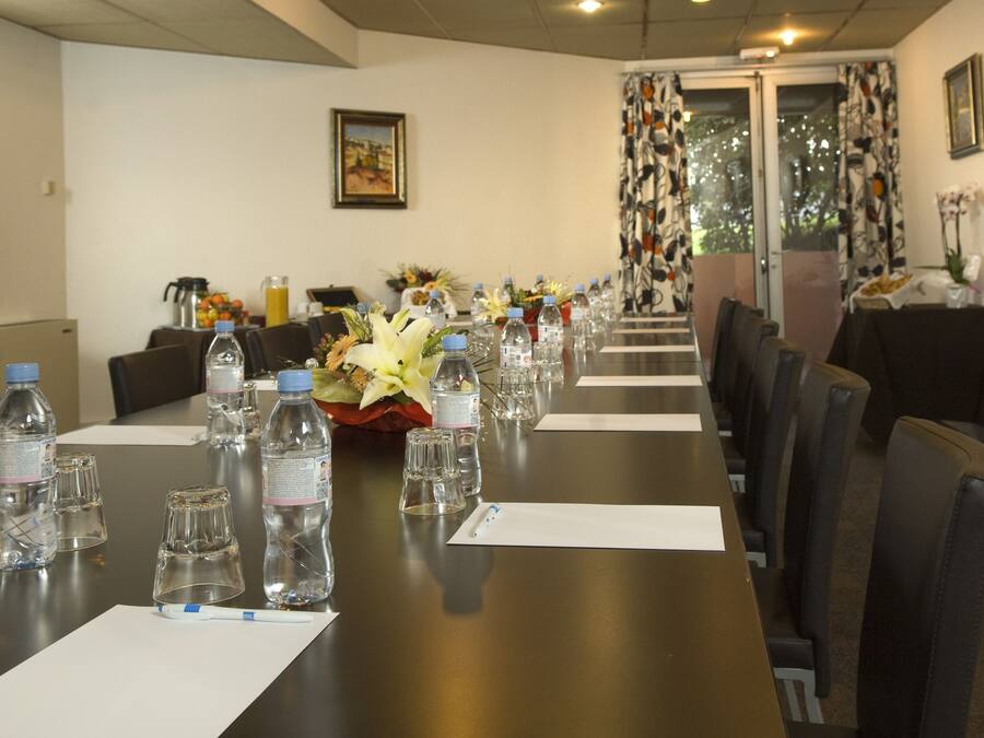 Uma sala de conferências com uma mesa comprida, cadeiras, garrafas de água e um arranjo floral.