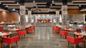 Um restaurante moderno com um balcão comprido, cadeiras estofadas em vermelho e piso de azulejos polidos.