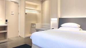 Quarto de hotel com cama, escrivaninha, guarda-roupa e banheiro.