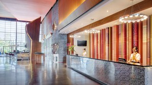 Uma área de recepção de hotel moderna, com divisória de vidro, um recepcionista e uma grande janela.