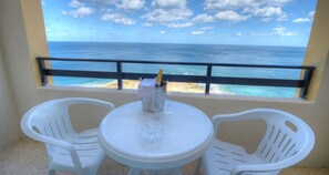 Uma varanda com mesa e duas cadeiras, com vista para a praia e o oceano.