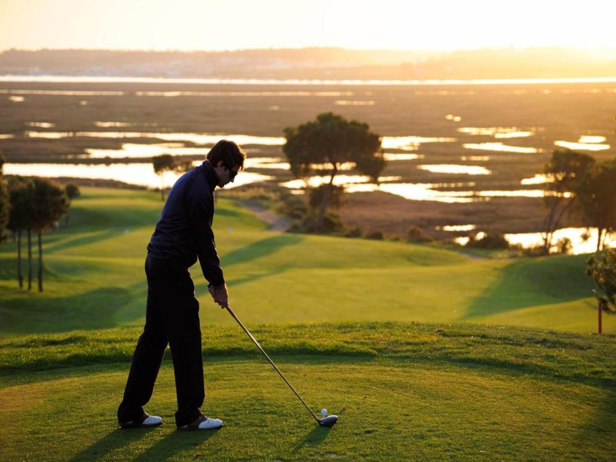 Uma pessoa jogando golfe em um campo com o pôr do sol ao fundo.