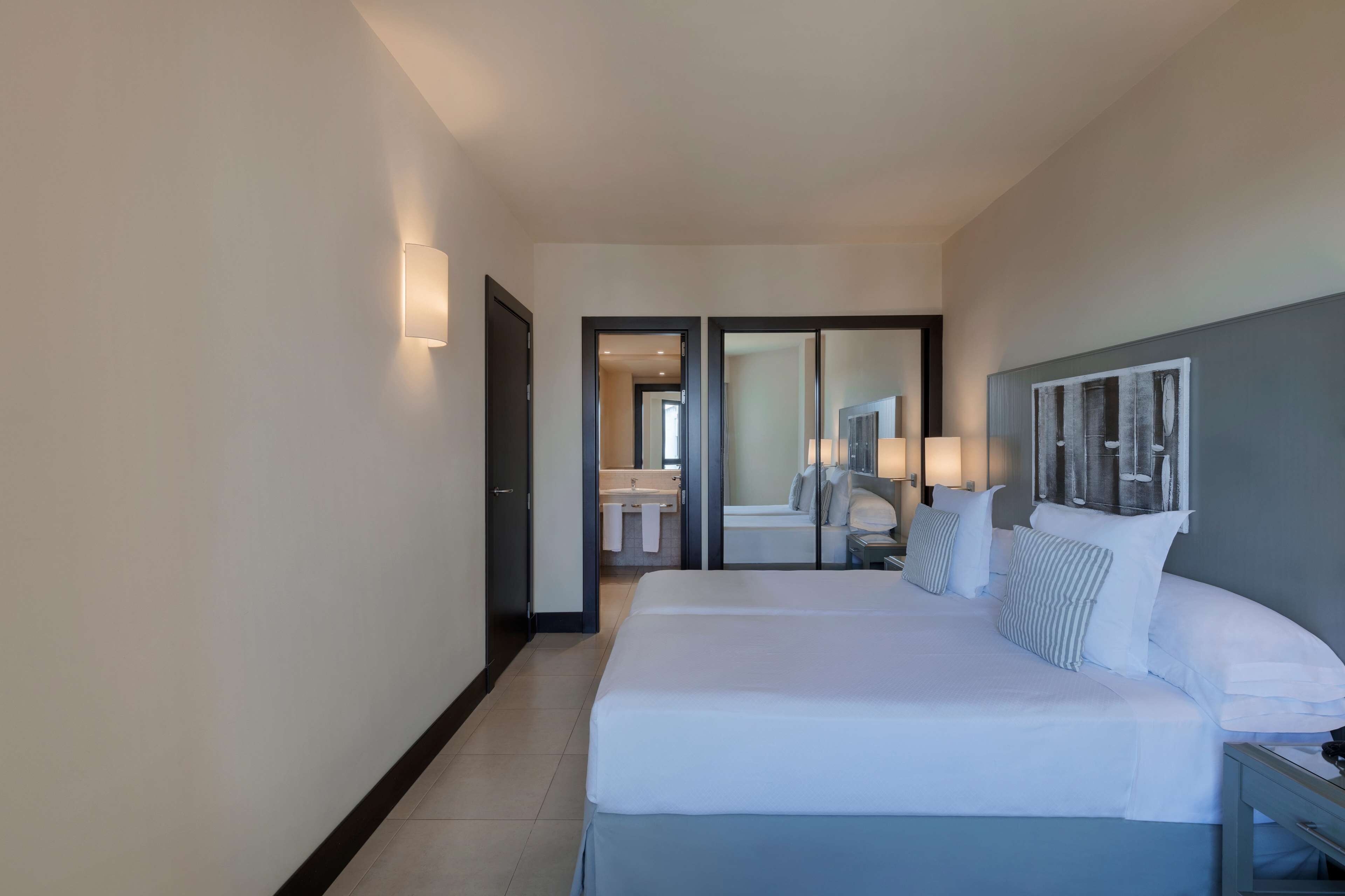 Quarto de hotel com uma cama grande, uma mesa de cabeceira, um espelho e vista para o banheiro.