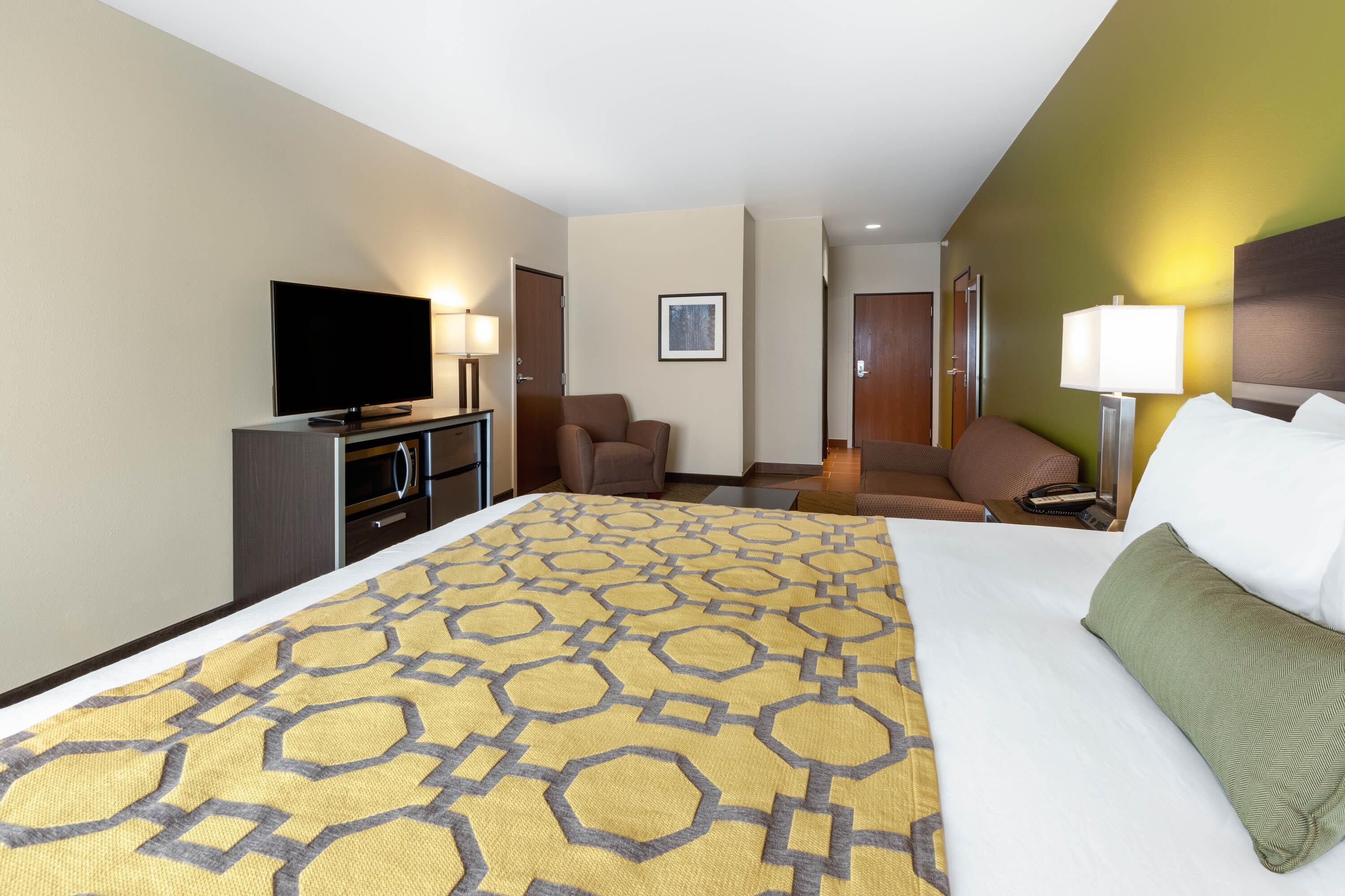 Quarto de hotel com uma cama grande, televisão, escrivaninha com abajur e uma cadeira.