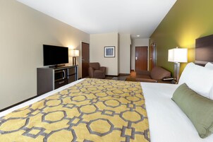 Quarto de hotel com uma cama grande, televisão, escrivaninha com abajur e uma cadeira.