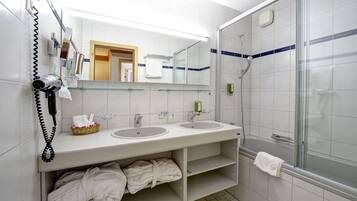 Casa de banho com duas pias, cabine de duche em vidro, secador de cabelo e espelho.