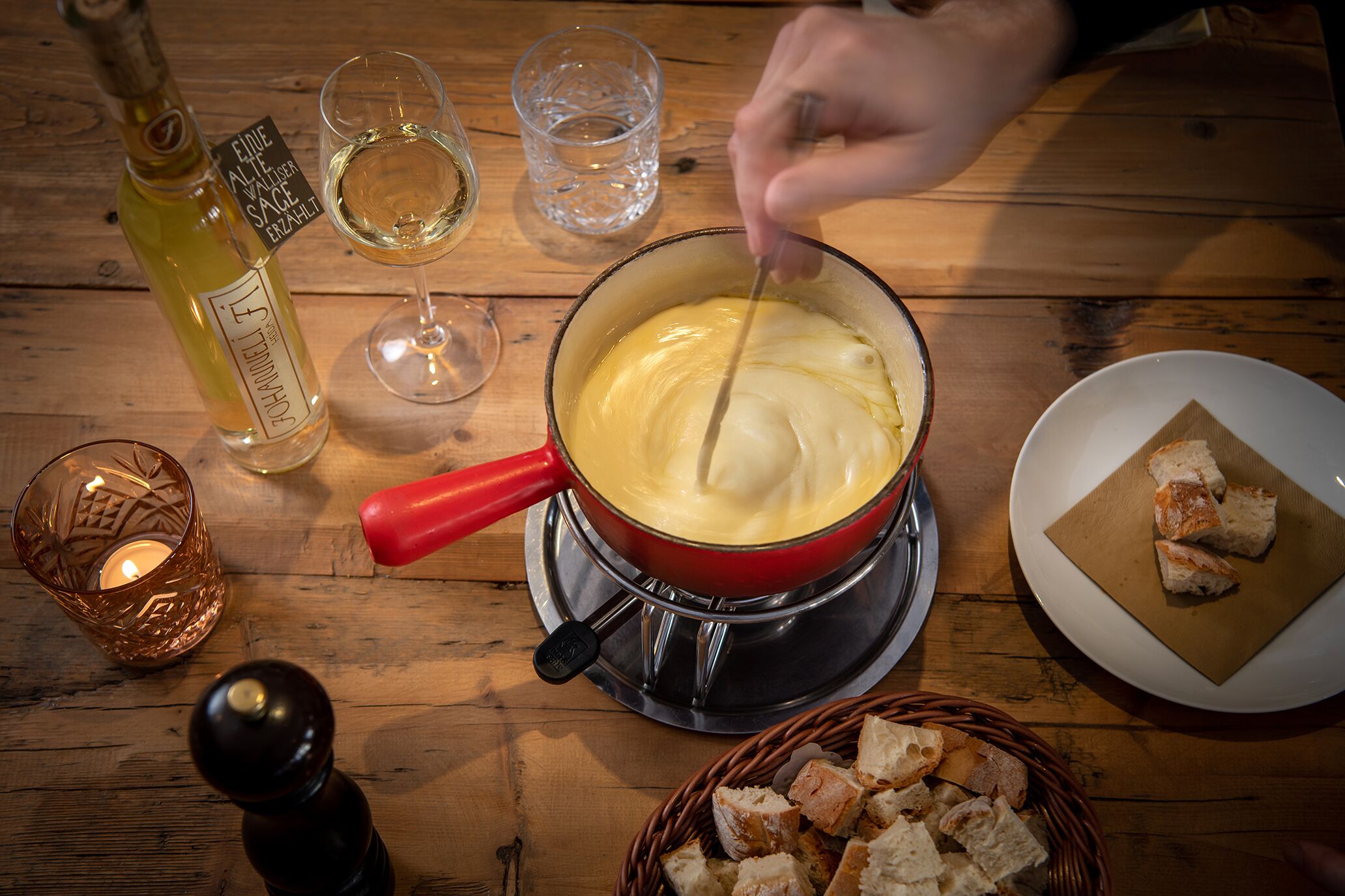 Uma mesa de madeira com uma panela vermelha, uma garrafa, copos e pão.