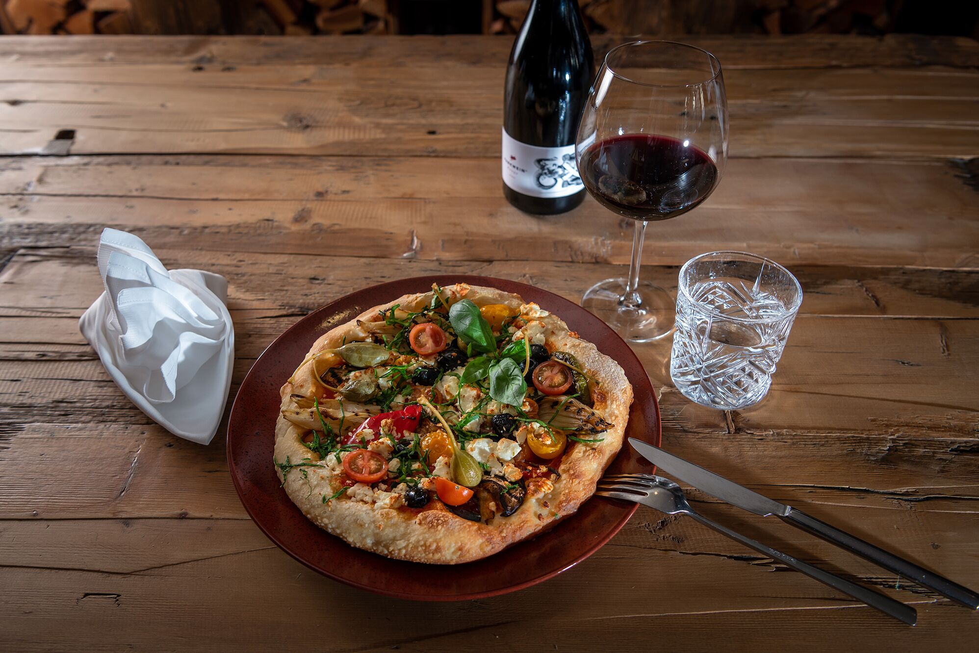 Pizza sobre uma mesa de madeira, com uma garrafa de vinho e copos.