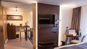 Quarto de hotel moderno com televisão de tela plana, uma mesa com um laptop, uma cadeira, uma cama e um pequeno espaço de estar.