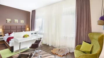 Quarto de hotel moderno com uma cama, escrivaninha, cadeira e uma janela grande com cortinas.