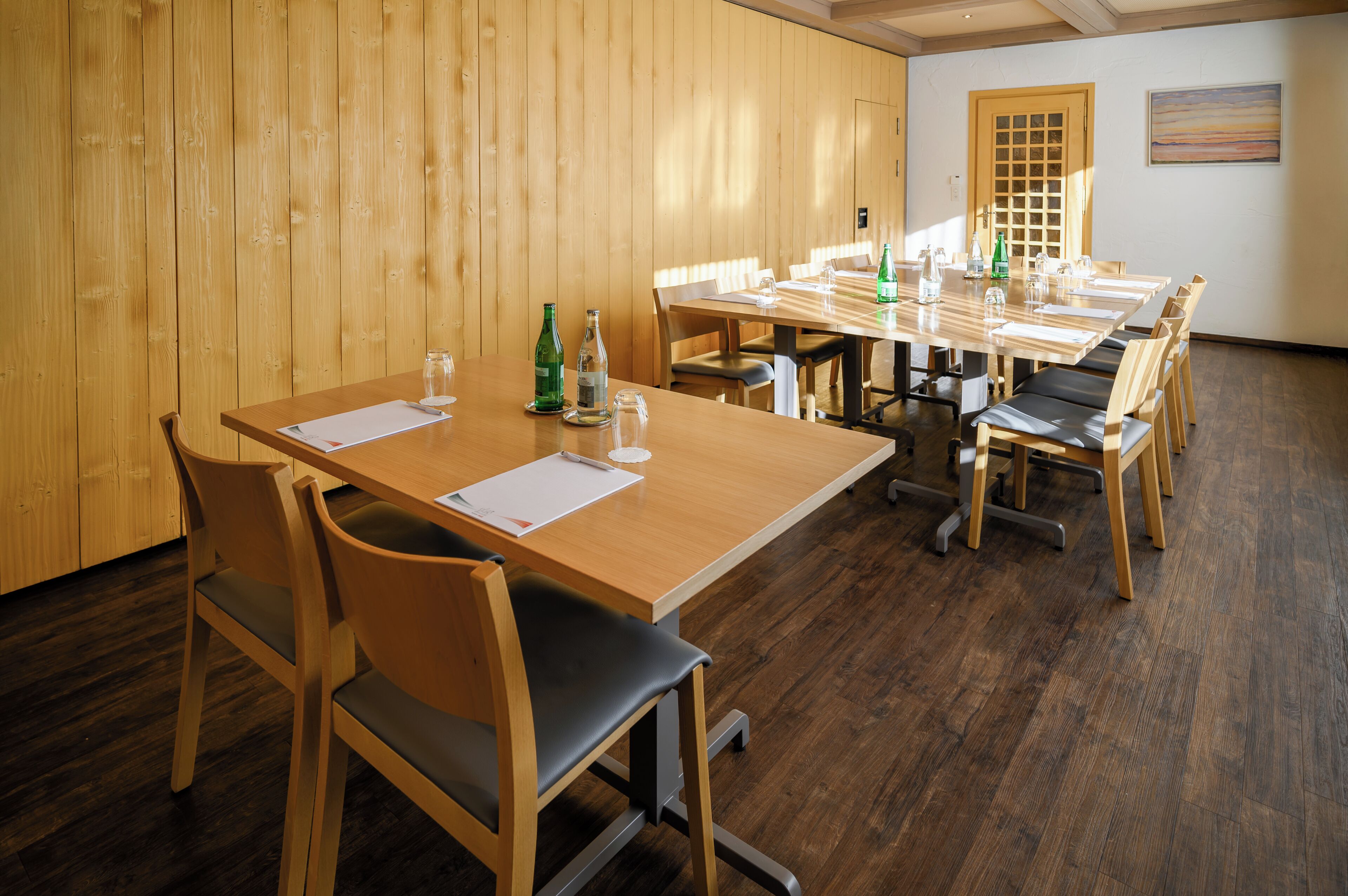 Sala de conferências com uma mesa comprida, cadeiras e painéis de madeira.