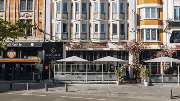 Um hotel com fachada clássica, várias varandas e área de café no térreo com mesas ao ar livre.