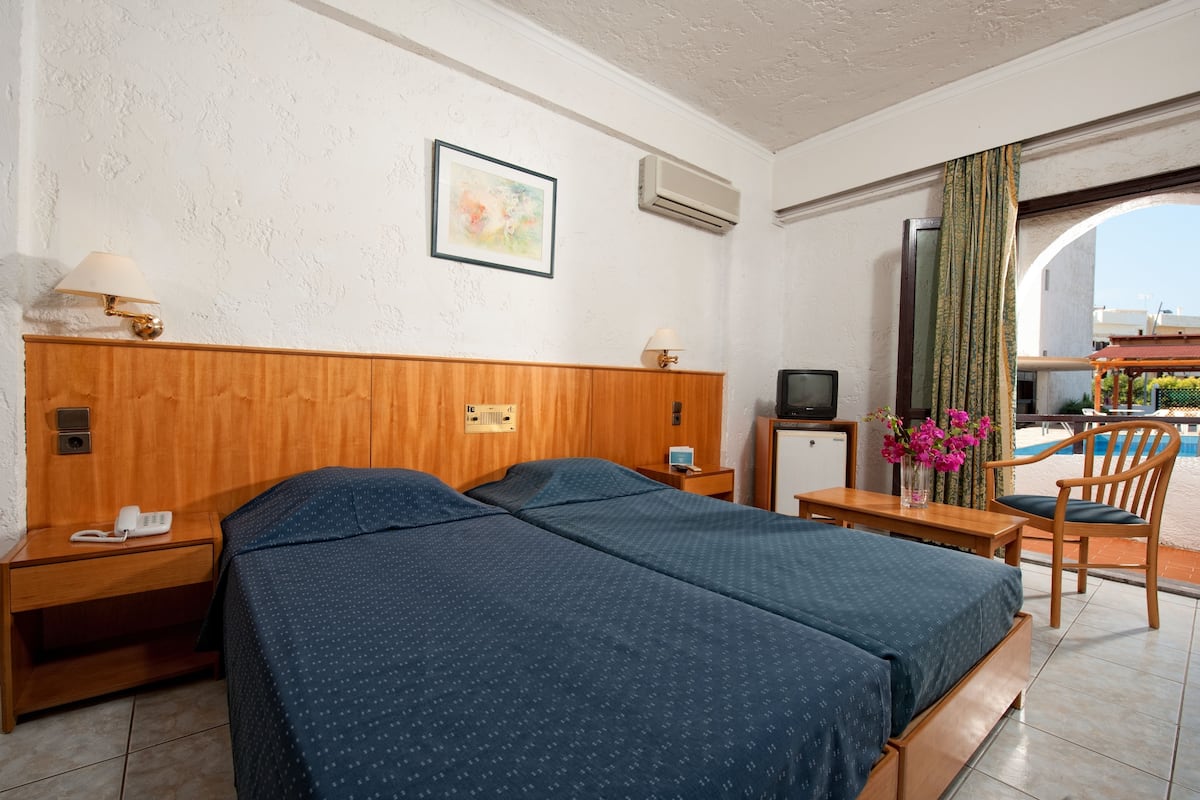 Quarto de hotel com duas camas, uma escrivaninha, uma cadeira, uma televisão e vista para uma piscina.