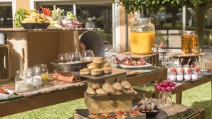 Uma mesa de buffet com diversos alimentos, incluindo batatas fritas, molhos e um grande jarro de suco de laranja.