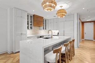 Uma cozinha moderna com armários brancos, uma ilha grande com banquetas e duas luminárias pendentes de vime.